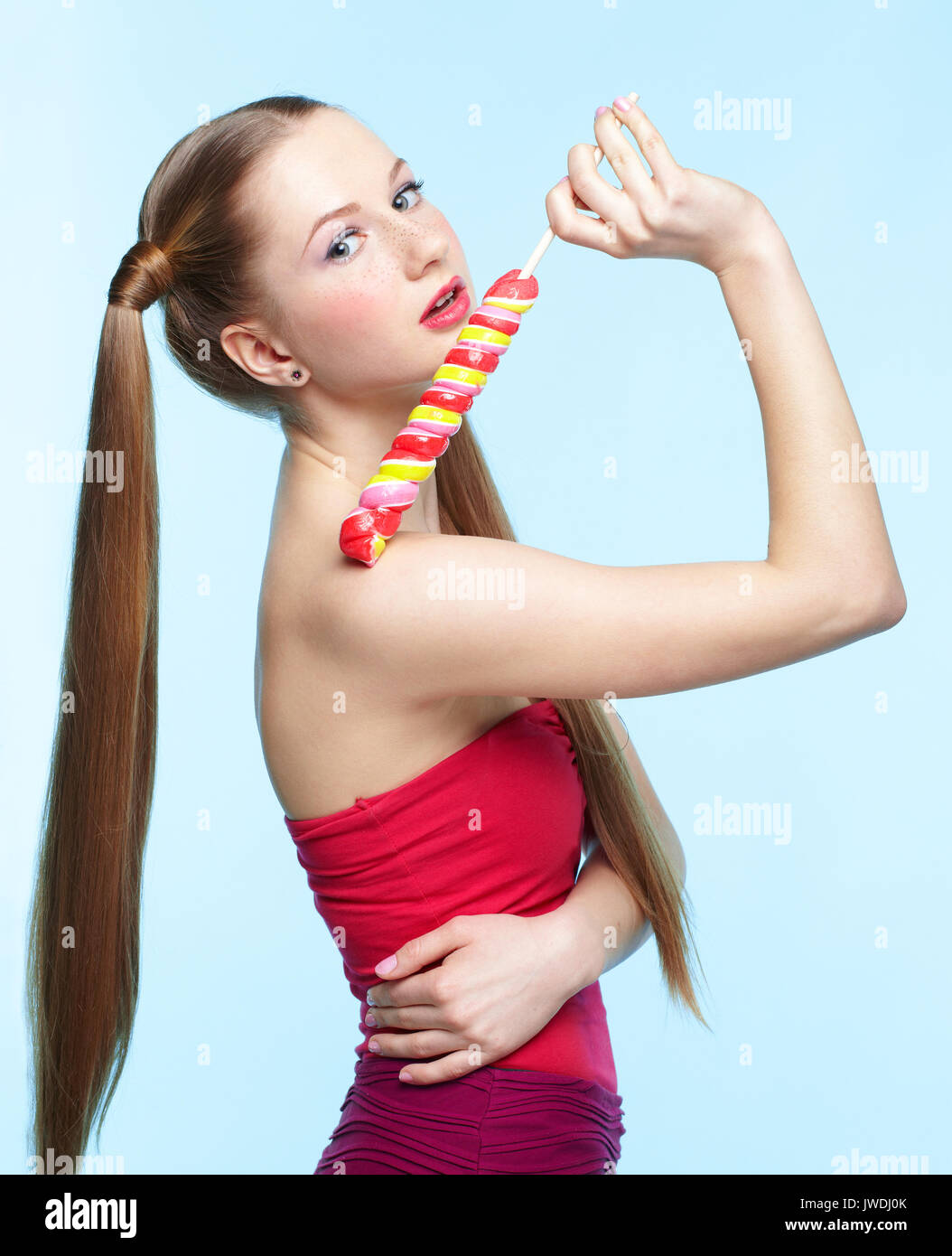Beautiful playful young freckled girl with lollipop on blue background ...