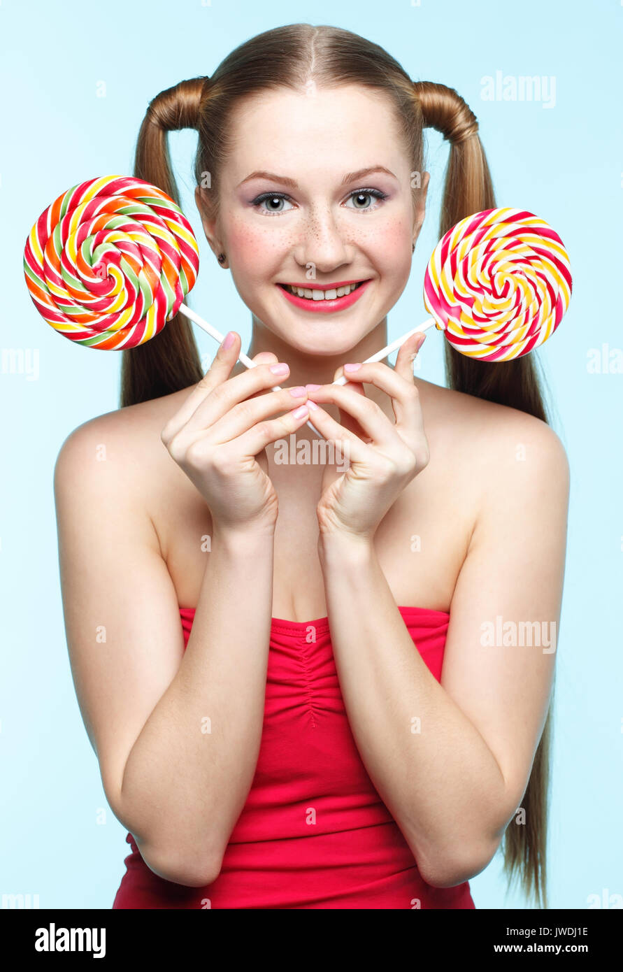 Beautiful playful young freckled girl with lollipop on blue background ...