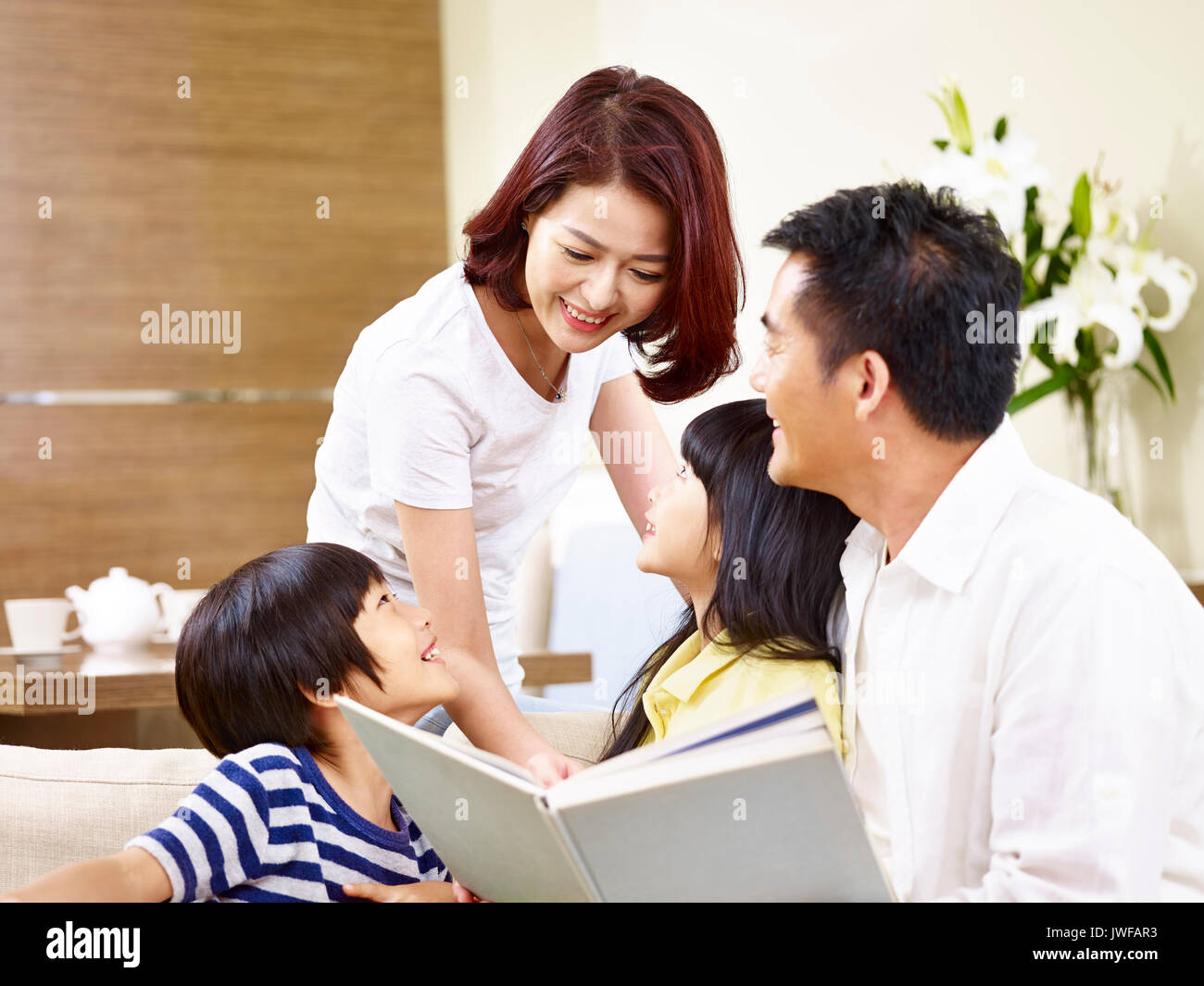 happy asian family with two children sitting on sofa reading a book ...