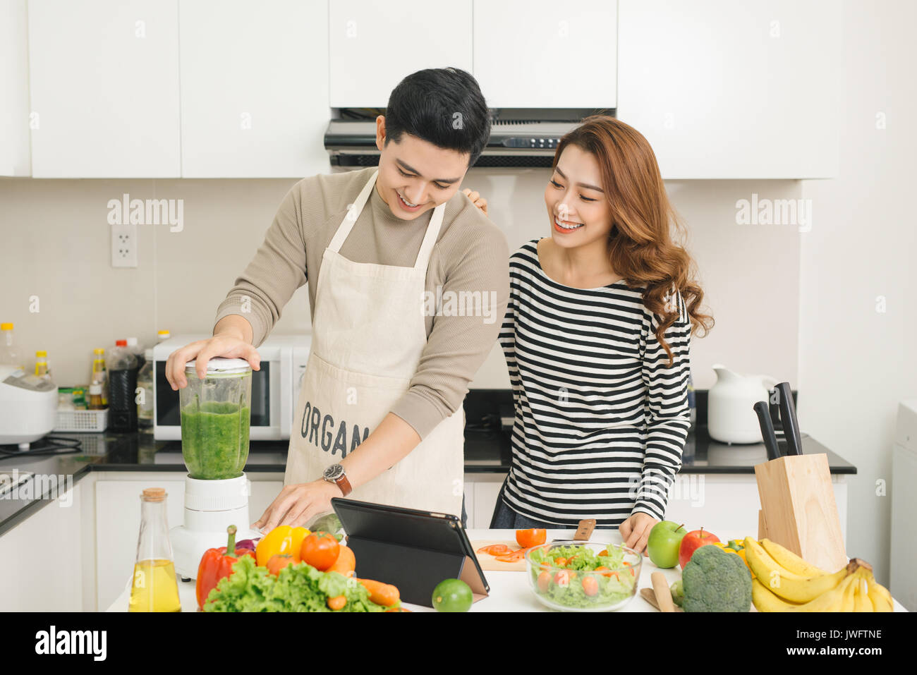 Portrait of happy asian young couple cooking together in the kitchen at ...