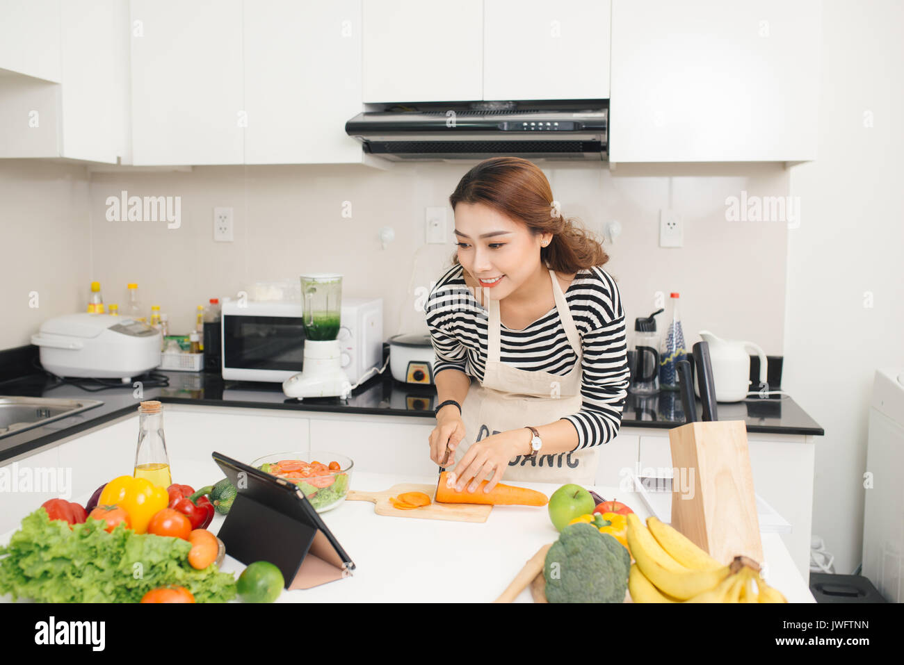 Beautiful asian woman cooking according to recipe on tablet screen ...