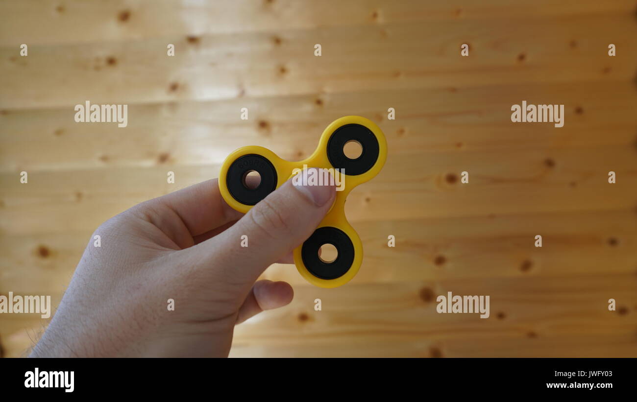 yellow hand spinner, or fidgeting spinner, rotating on child's hand ...