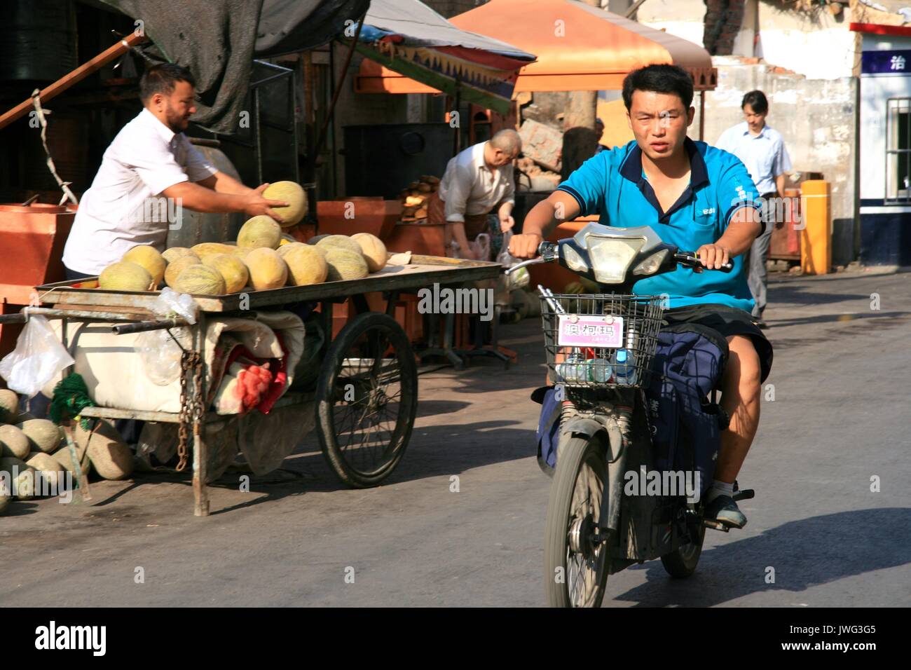 Man riding motorbile in front of melon stall in the Urumqi old market ...
