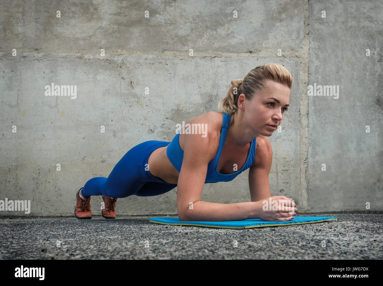 woman doing plank exercise against the background of a concrete wall ...