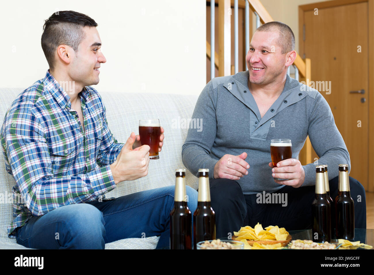 Cheerful adult men drink beer at home on a day off.Focus on the right ...