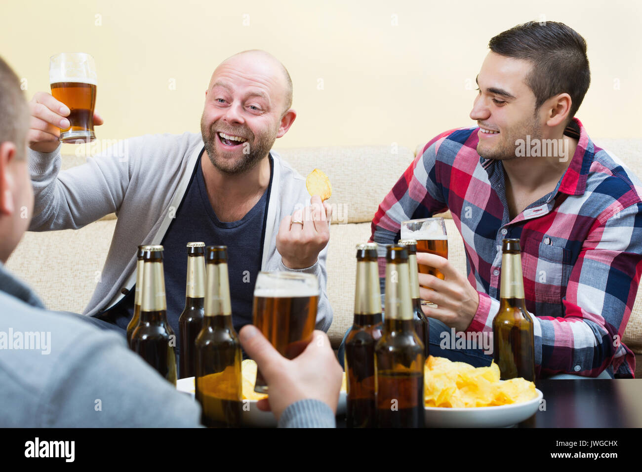 Three adult smiling men sitting at table and discussing something ...