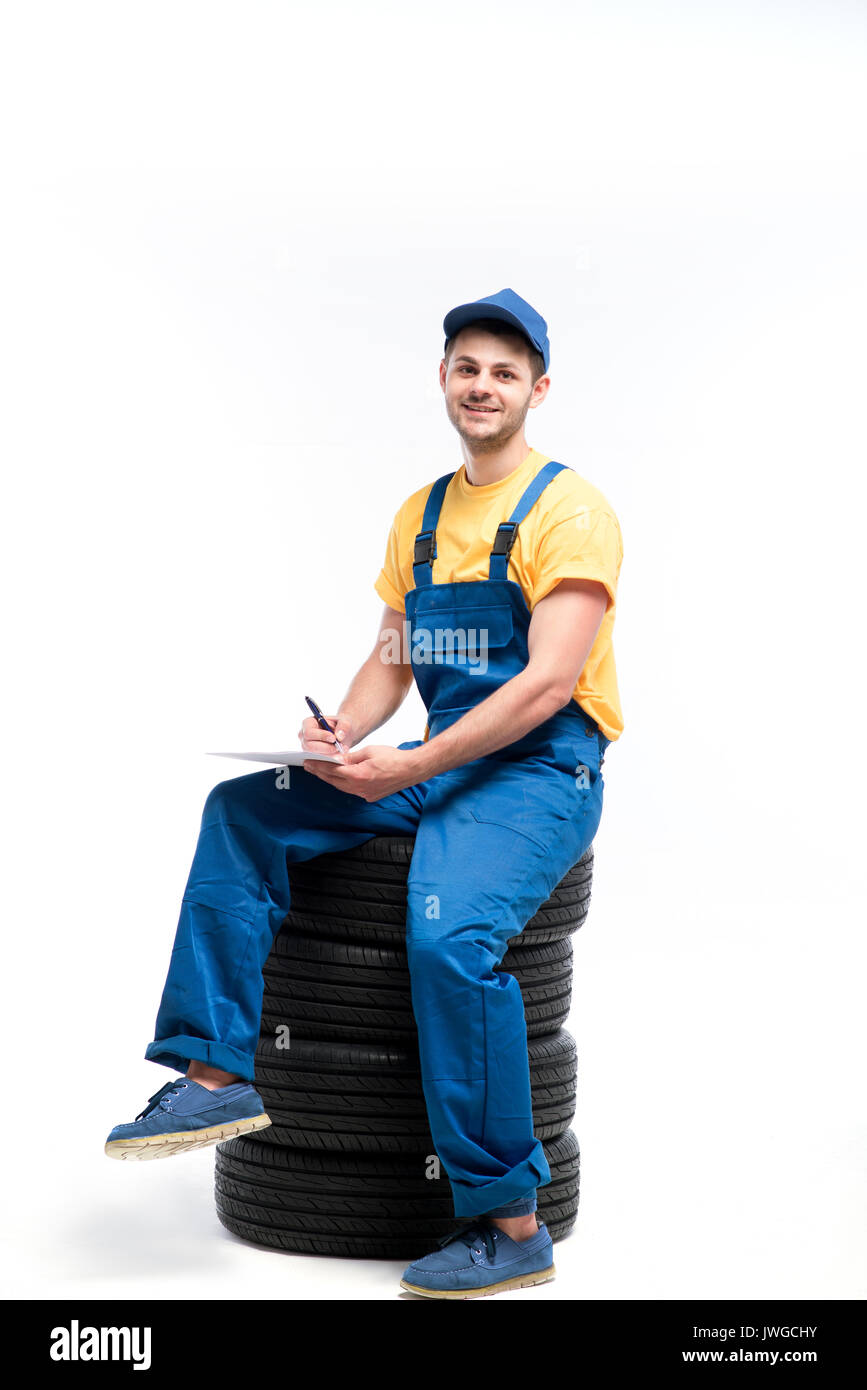 Tyre service worker sitting on a pile of tires, white background ...