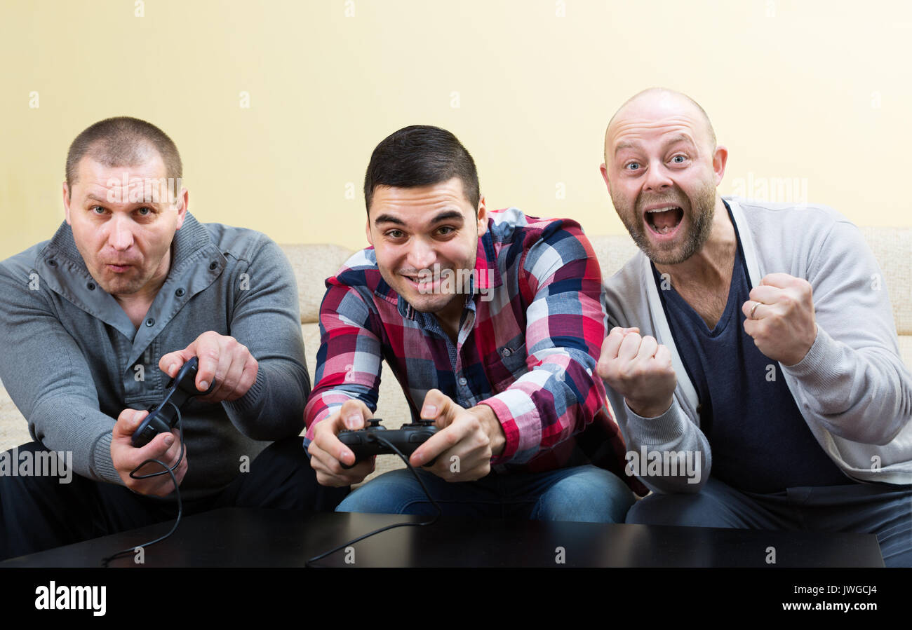 Three shouting friends playing video games at apartment party Stock ...