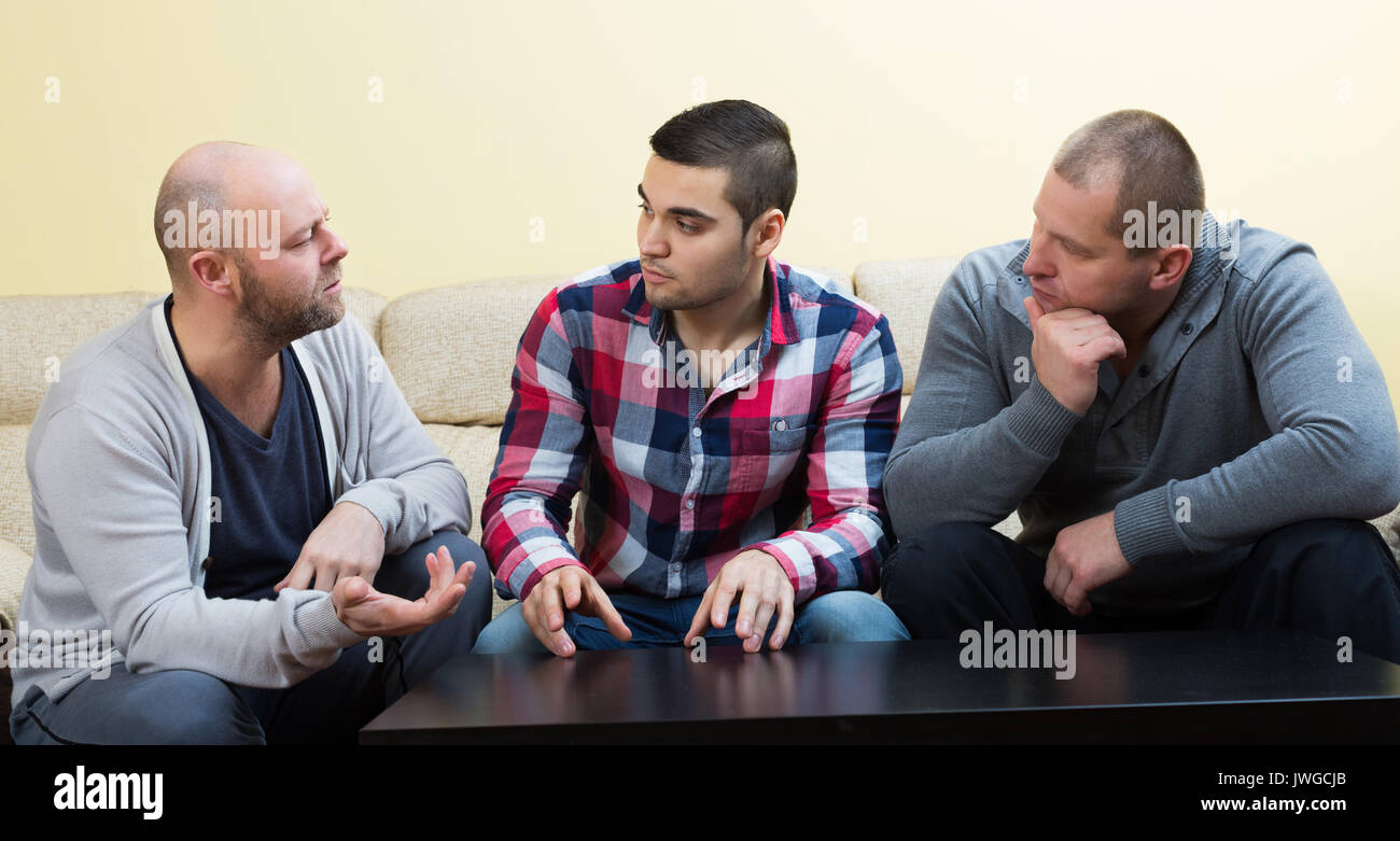 Three males having a serious conversation at living room Stock Photo ...