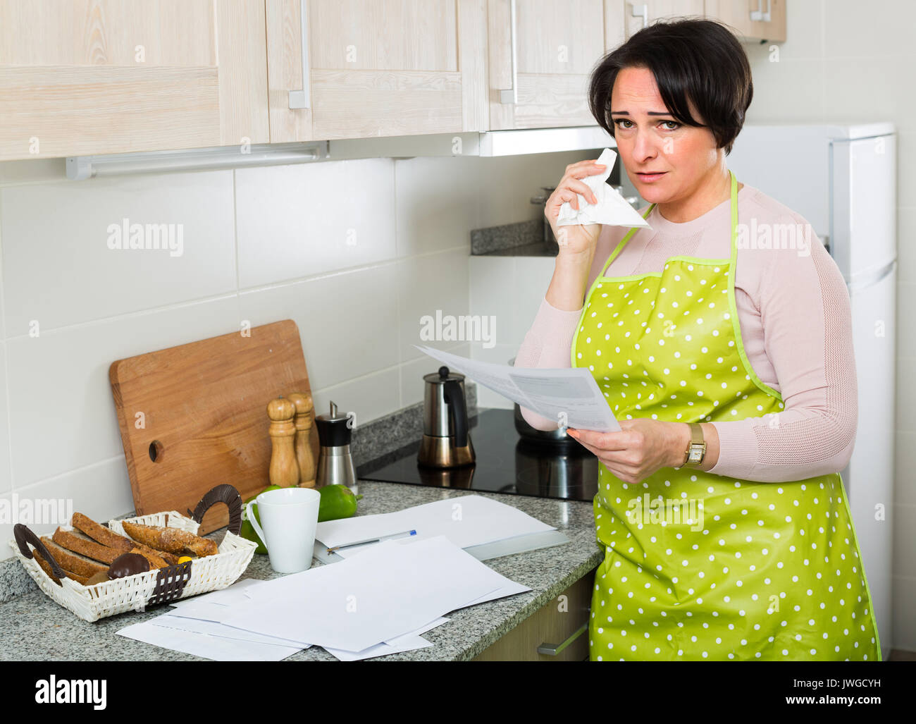 Sad woman looking through financial documents and crying at home ...