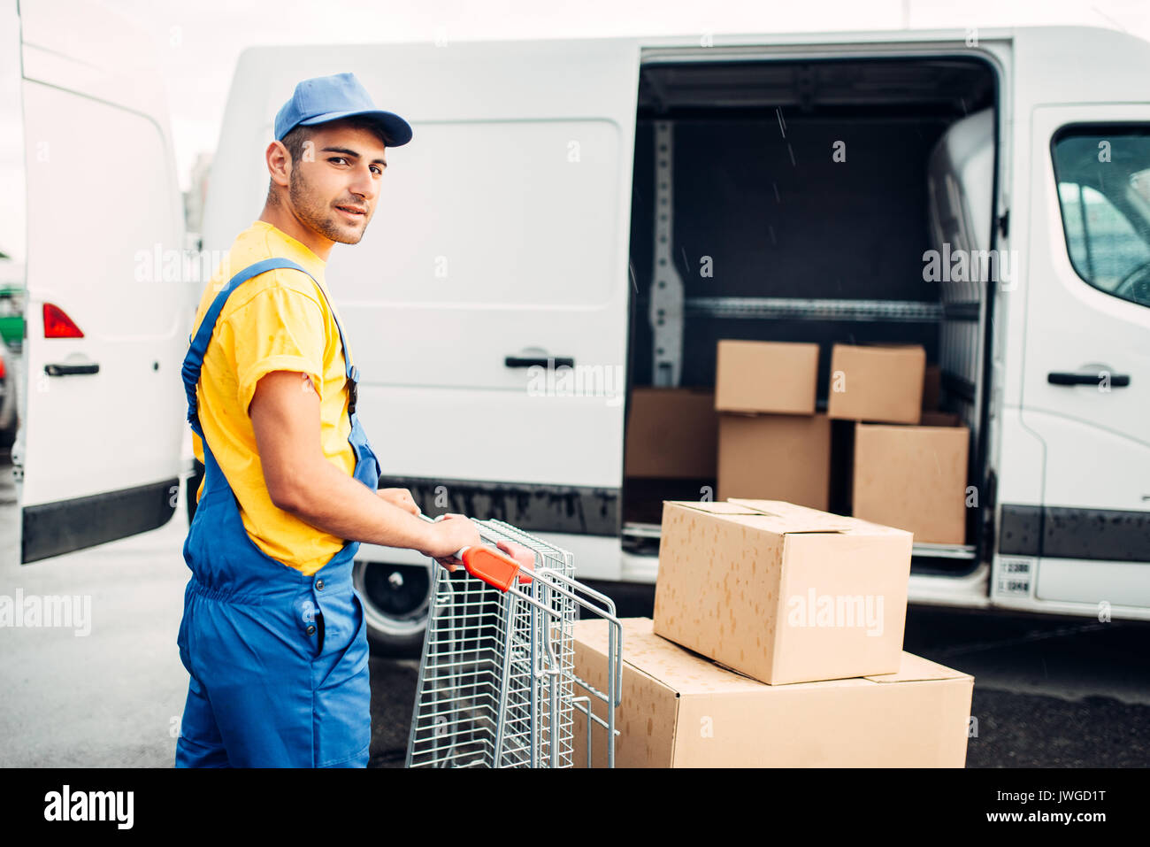 Male courier in uniform works with cargo, back view. Truck with parcels ...