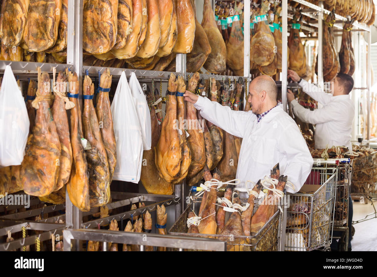 Mature butcher and his young assistant with jamon joints at a meat ...