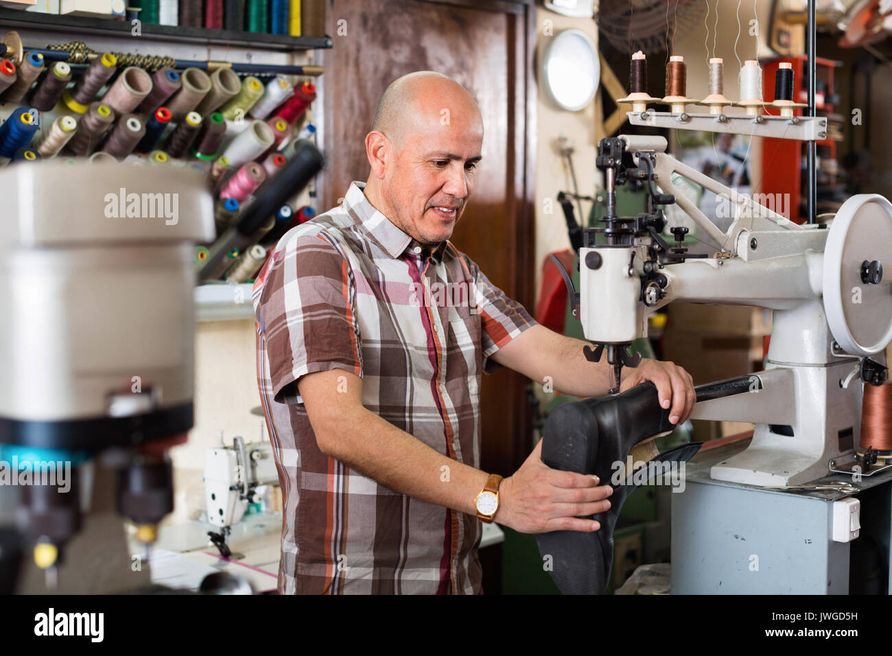 Mature efficient positive workman sewing leather boots on stitch lathe ...