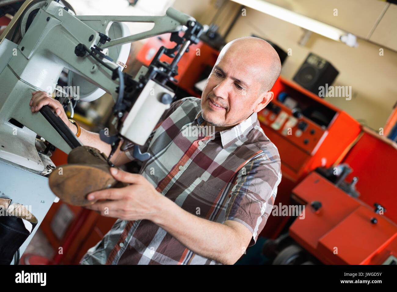 Mature diligent positive workman sewing leather boots on stitch lathe ...