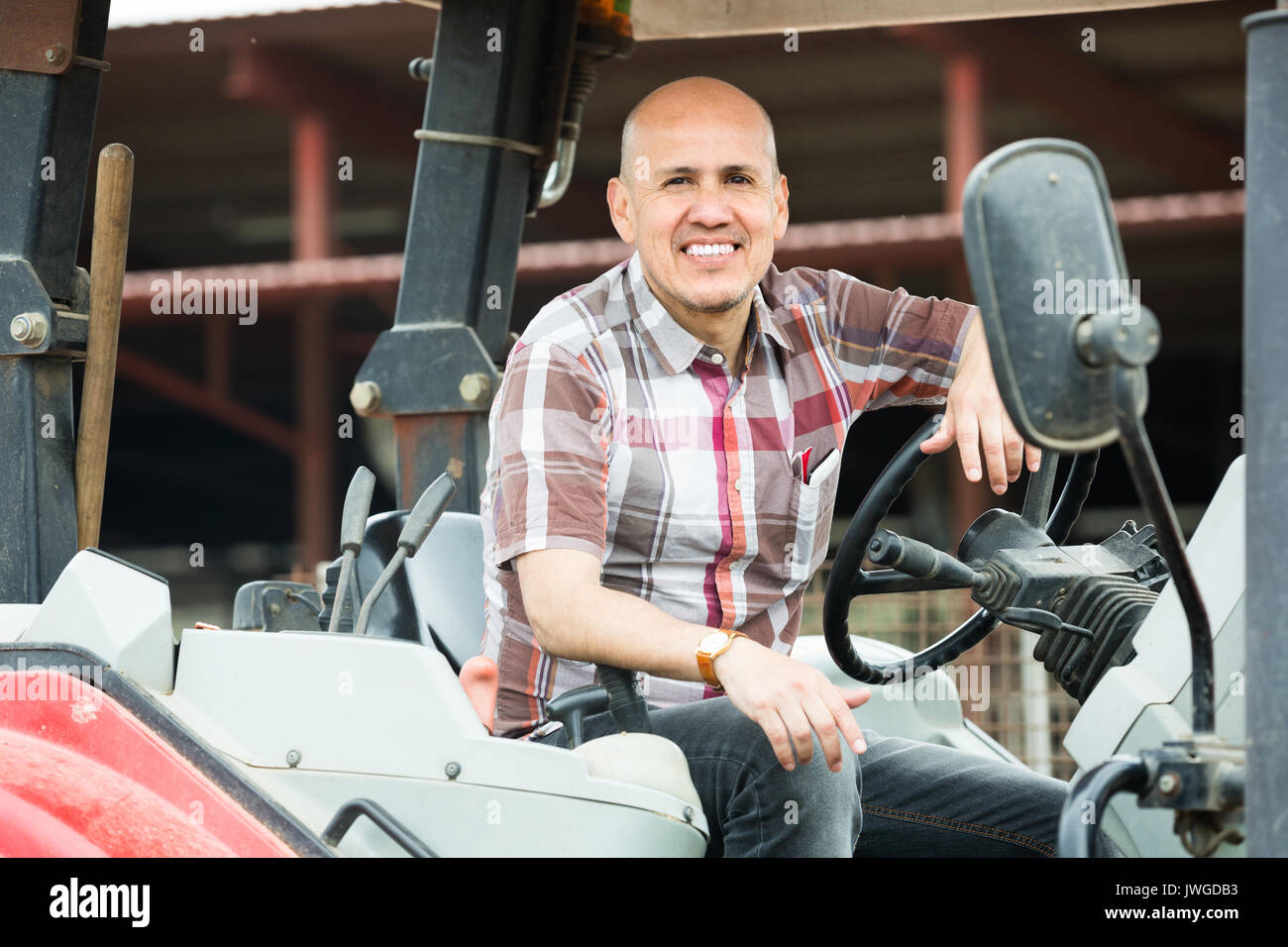 Mature male driver operating modern tractor in livestock farm outdoor ...