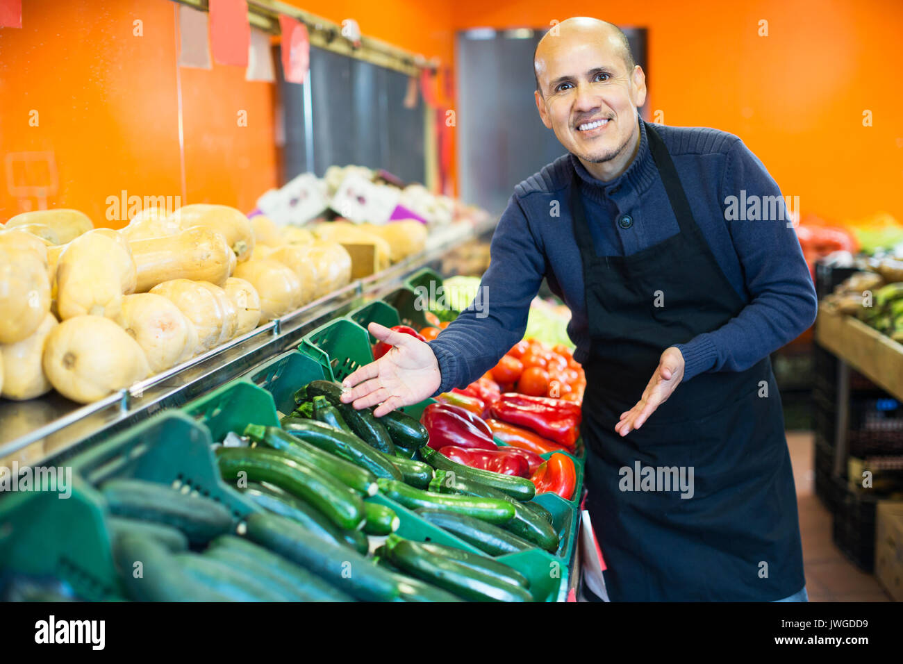 Portrait of salesman posing near display with different vegetables in ...