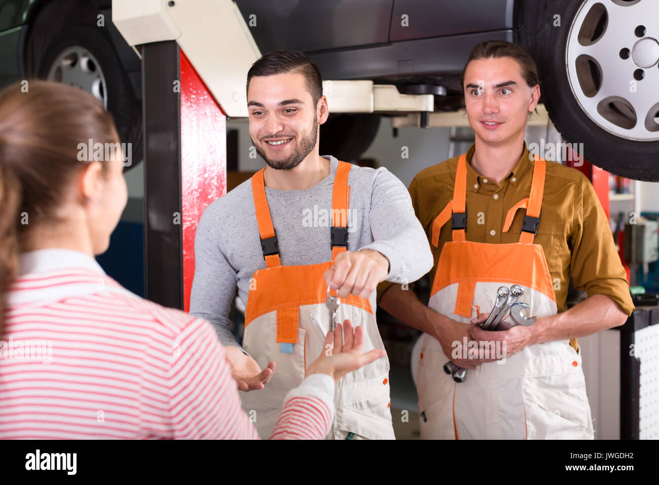 Smiling automobile service crew in white and orange uniforms handing ...