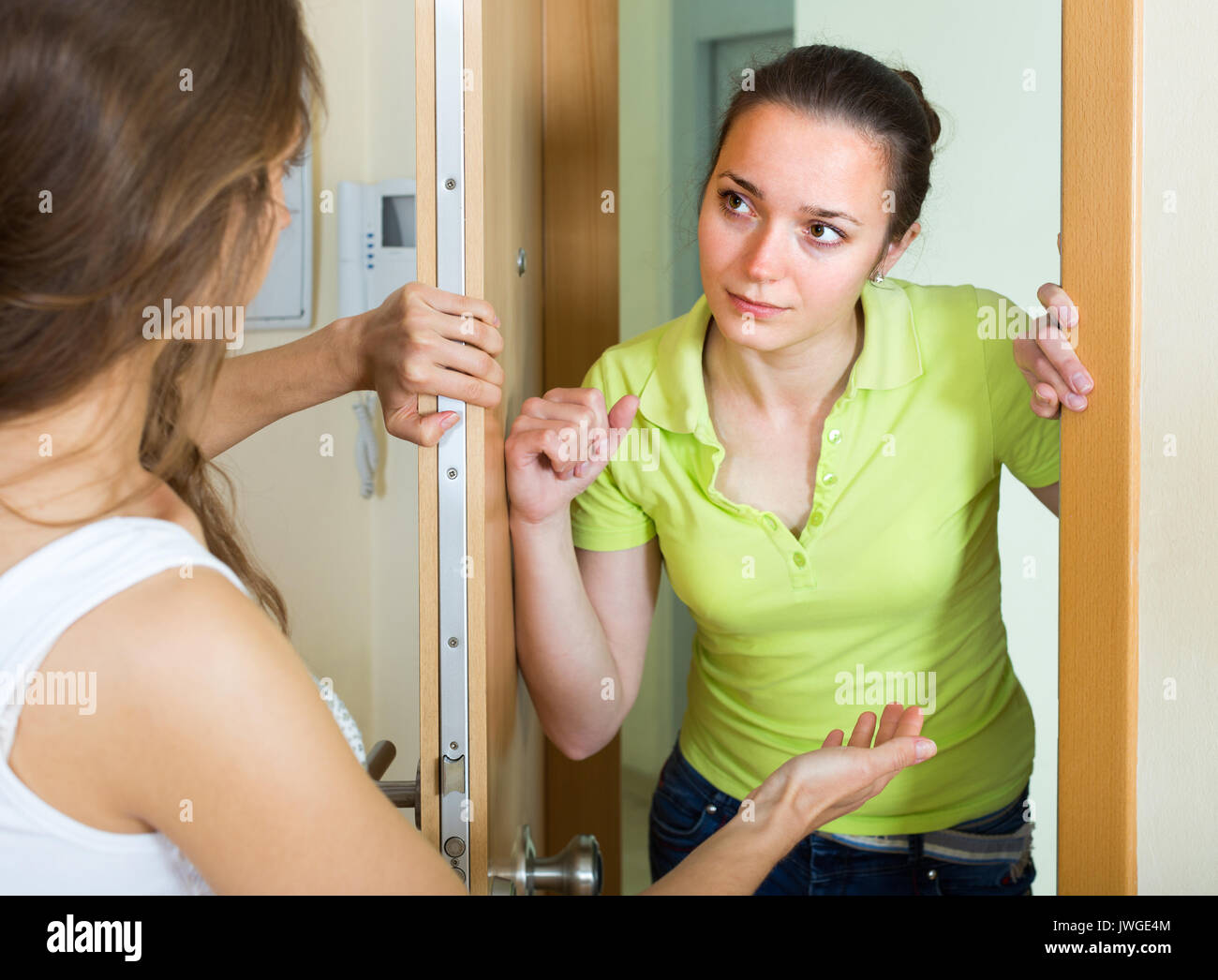 Two displeased young female neighbours having conflict at the door ...