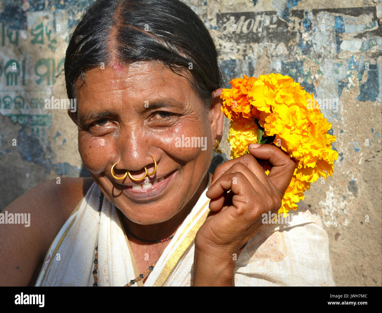 Indian Adivasi flower seller with three golden nose rings shows her ...