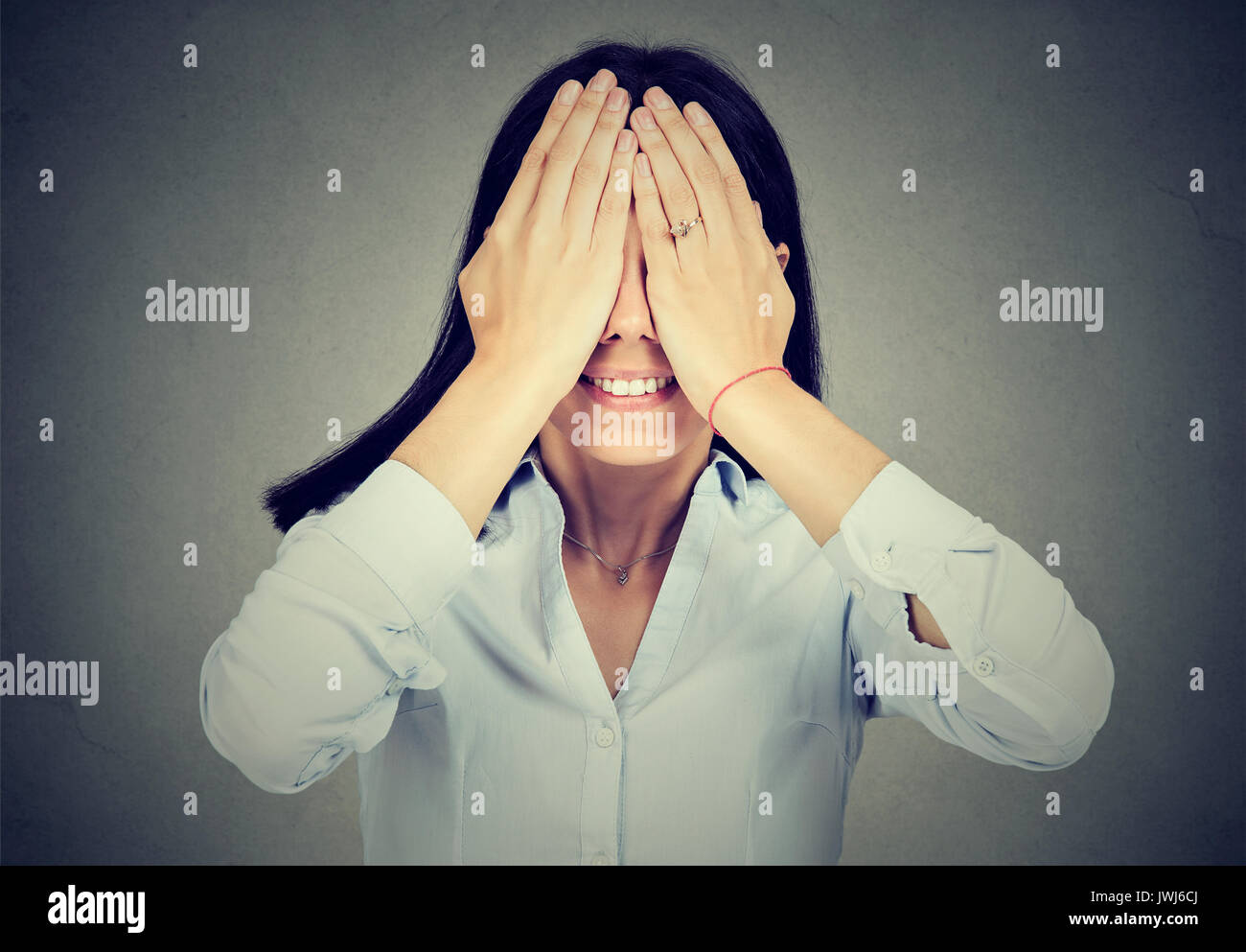 Portrait of a smiling woman covering her eyes isolated on gray ...