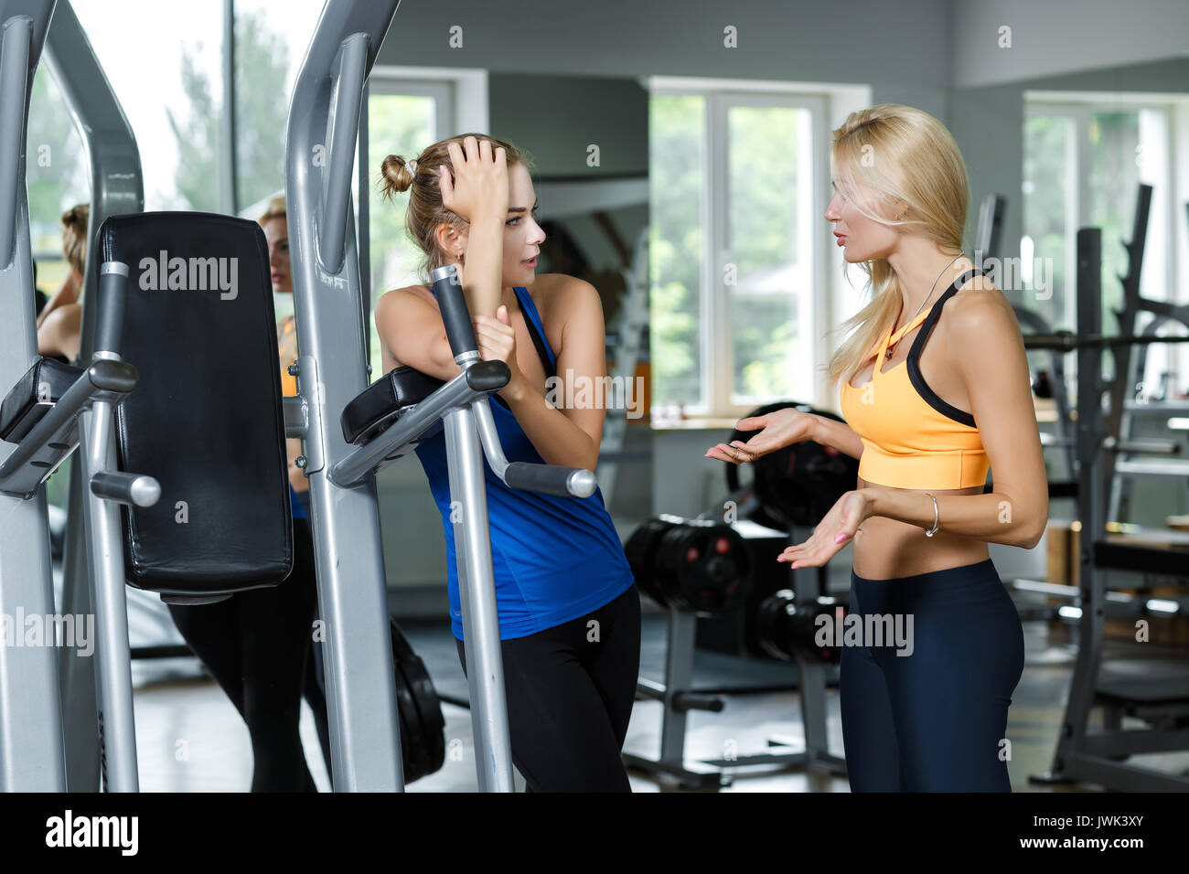 Two athletic blond women talking in the gym. Girl communicates with the ...