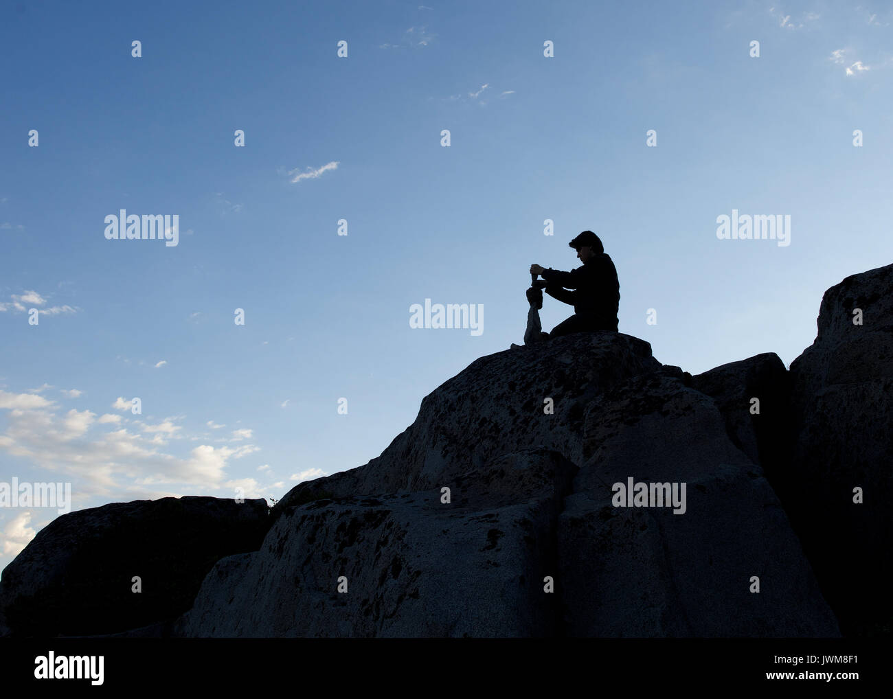 Silhouette of man making a sculpture with rocks on a mountain against ...