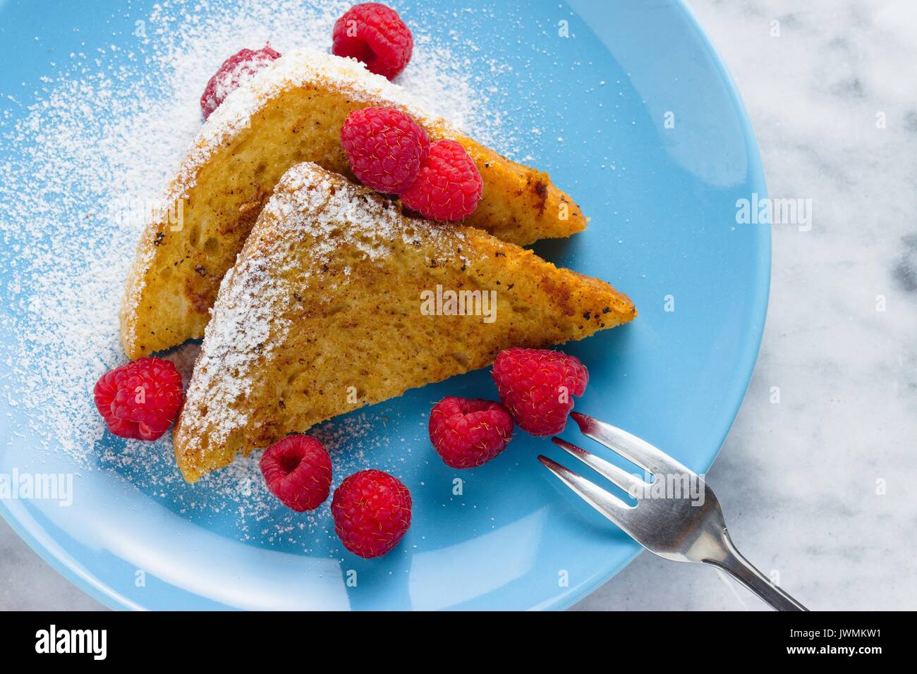 Two halves of bread slice fried into french toast, with raspberries and ...