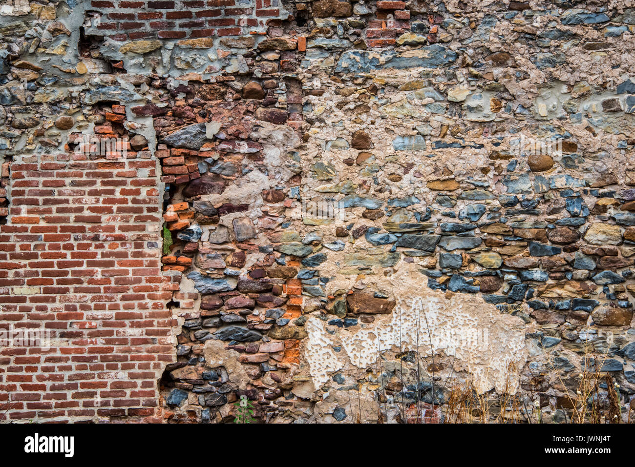 Old dilapidated stone wall with partial brickwork and missing or ...