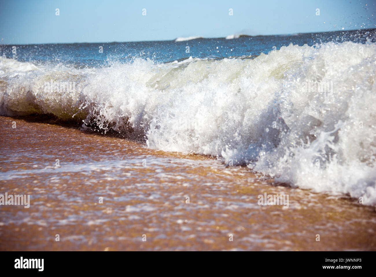 Sea wave splashing while breaking on the beach in a sunny day of summer ...