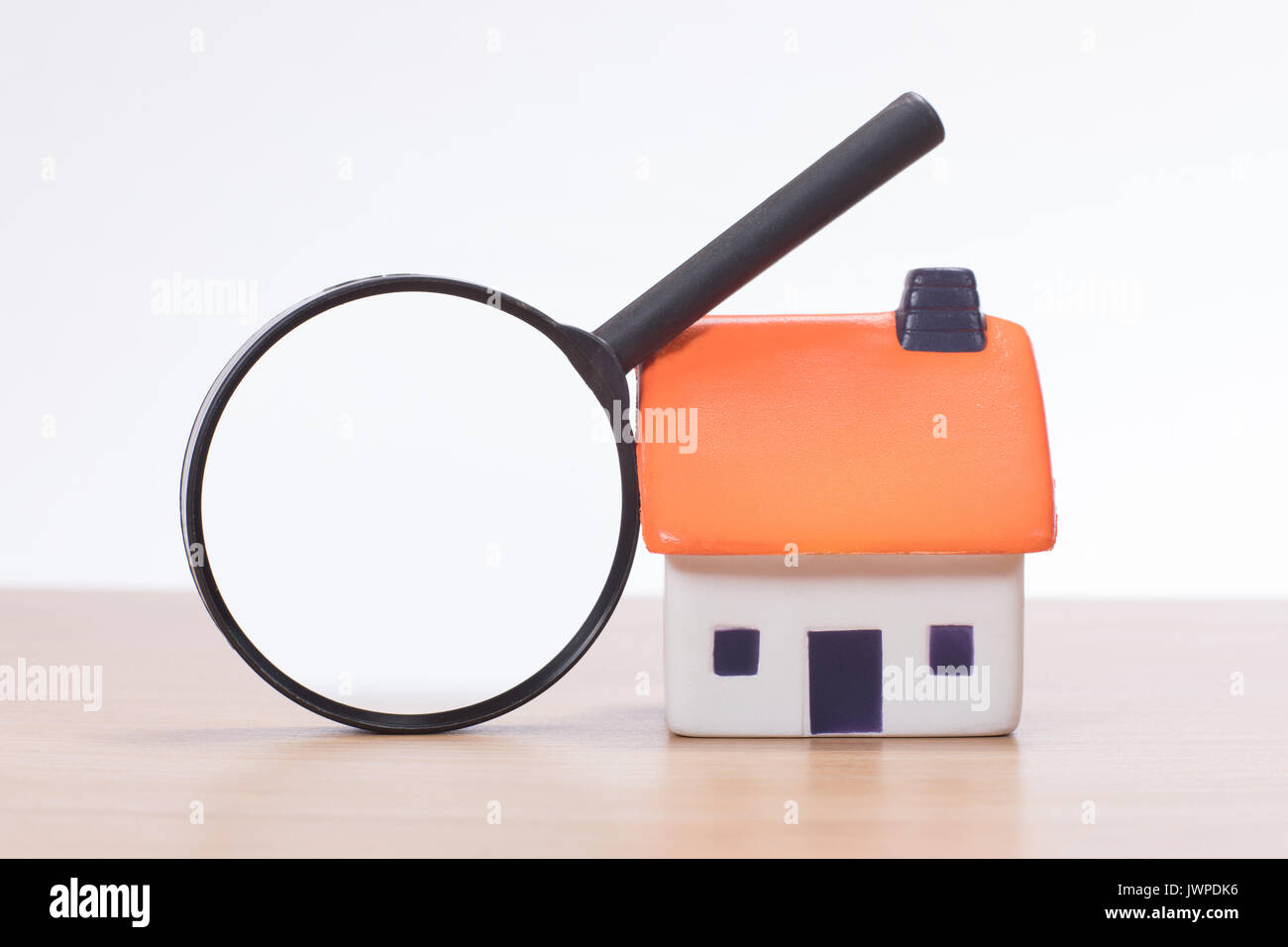 Magnifying glass leaning against house miniature on plain background ...