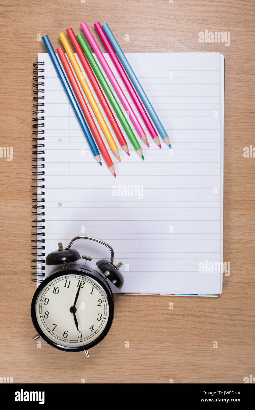 Colored pencils with alarm clock lying against blank spiral binder ...