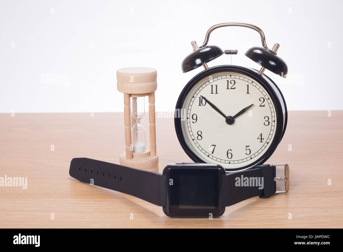Alarm clock with sandglass and digital watch standing on desk against ...
