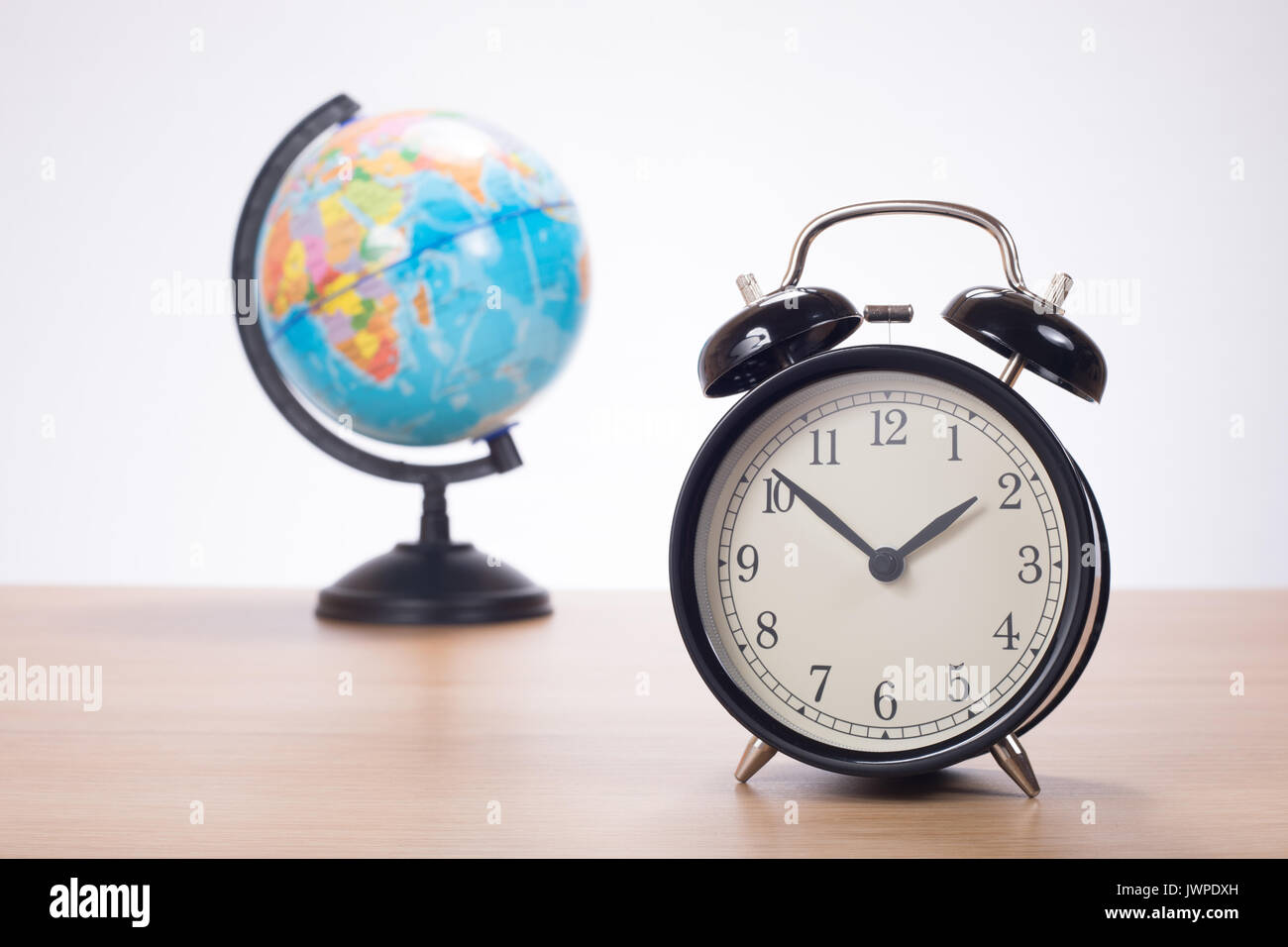 Alarm clock standing on desk against globe and plain background Stock ...