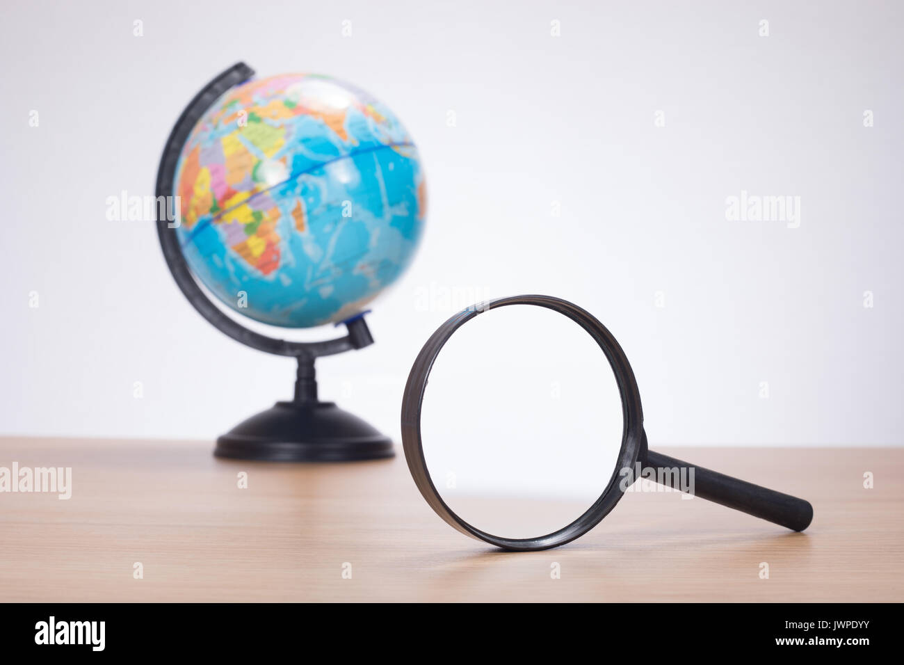 Magnifying glass with globe standin on desk against plain background ...