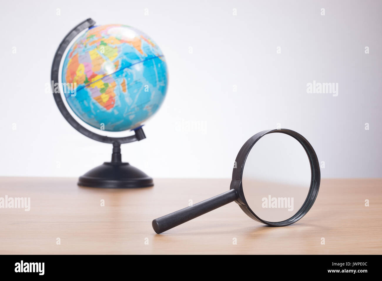 Side view of black magnifying glass and small multicolored globe on ...