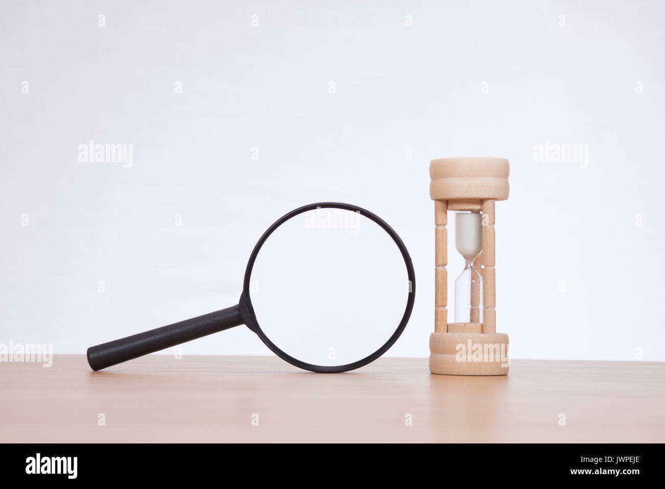 Magnifying glass with sandglass on desk against plain background Stock ...