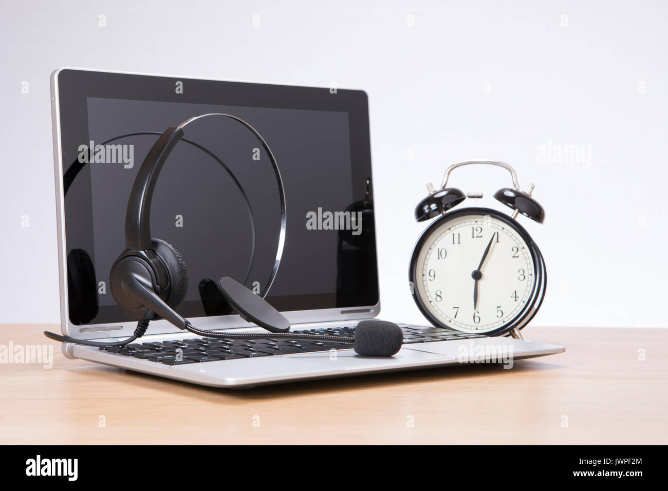 Alarm clock standing by laptop with headset on desk against plain ...