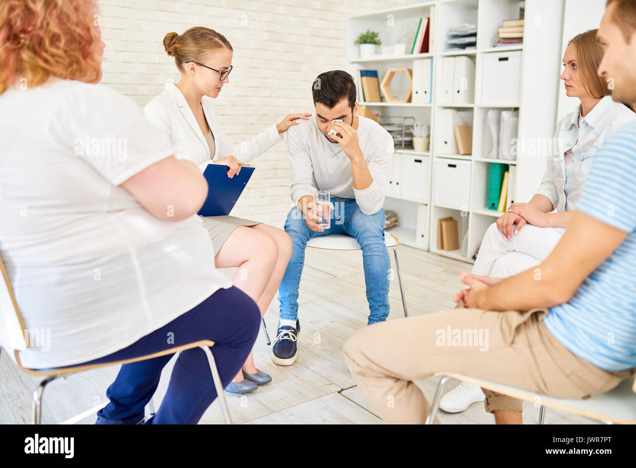 Portrait of young man crying in support circle of group therapy meeting ...