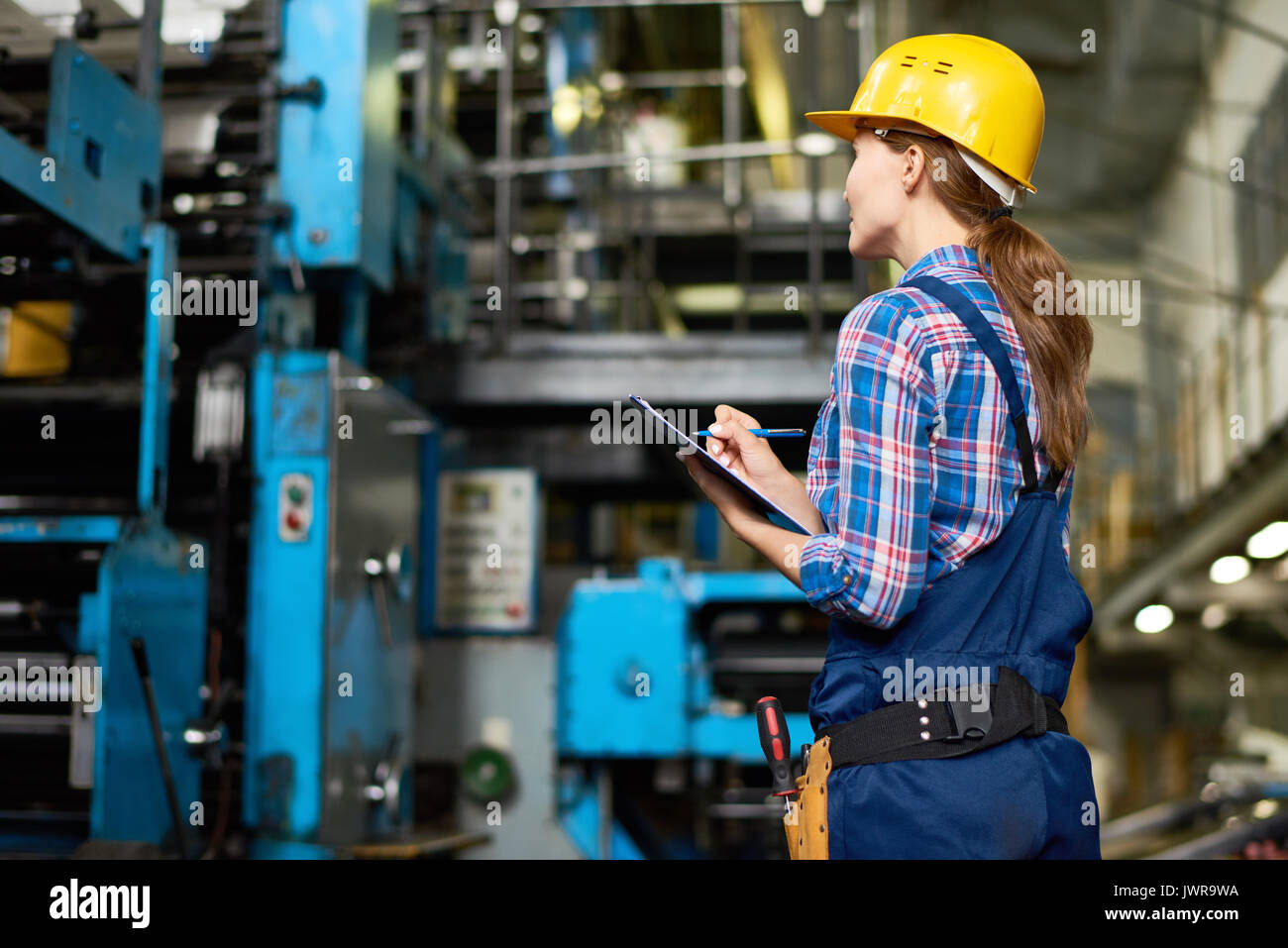 Portrait of female factory worker writing on clipboard while checking ...