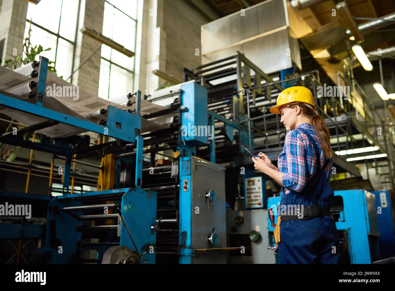 Portrait of female factory worker writing on clipboard checking ...
