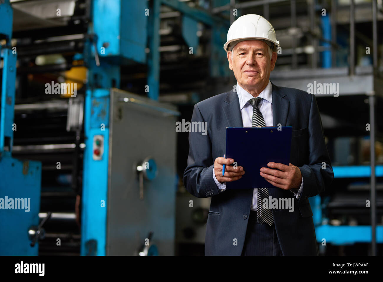Portrait of senior factory owner wearing hardhat on tour in modern ...