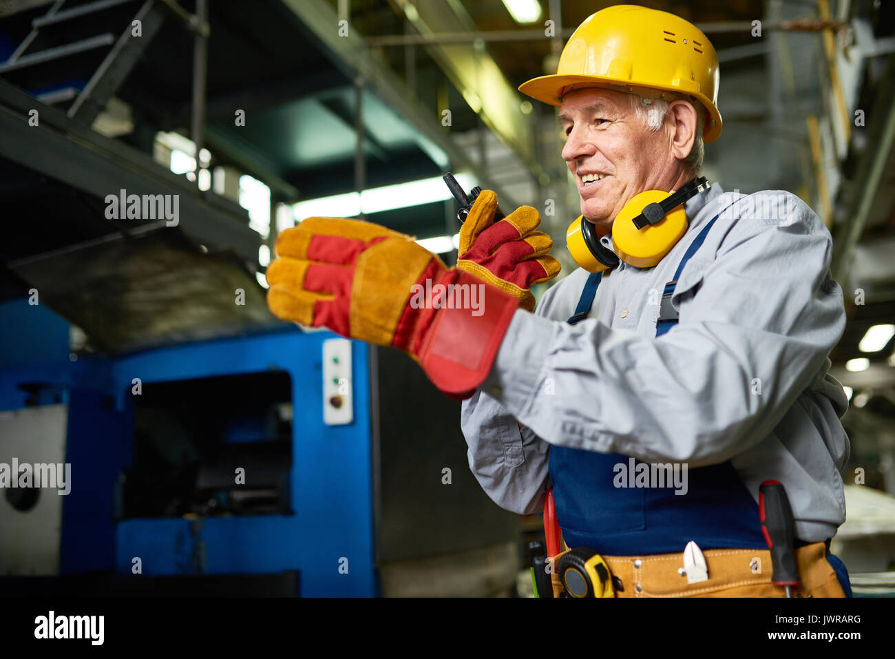 Portrait of senior factory worker using portable radio set and smiling ...