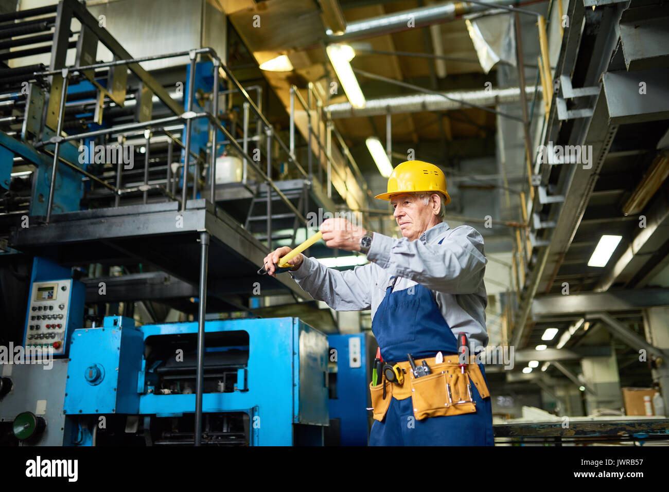 Portrait of senior mechanic checking measurements with reel tape while ...