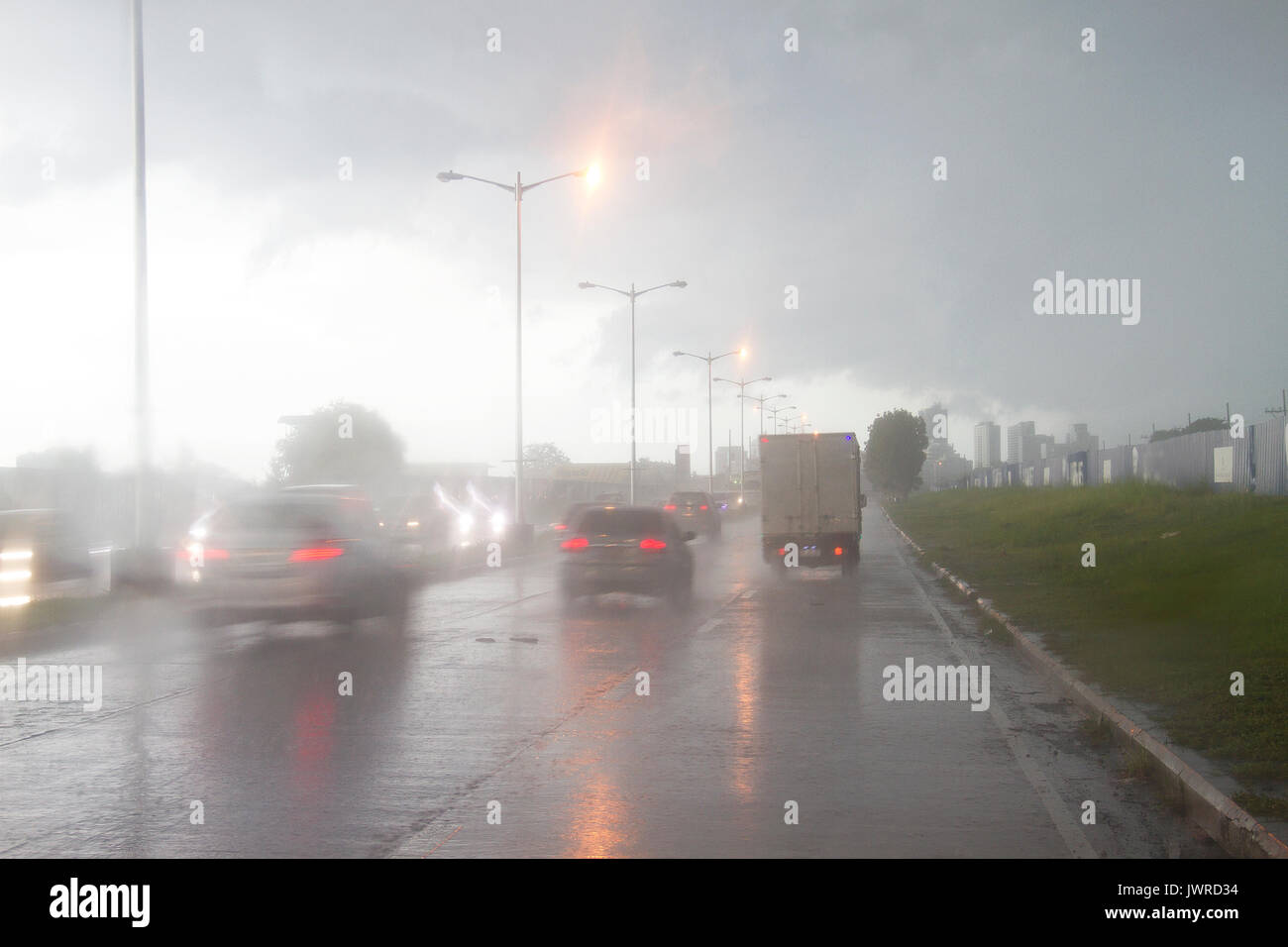 Heavy pouring rain thunder storm in a highway with buildings and dark ...