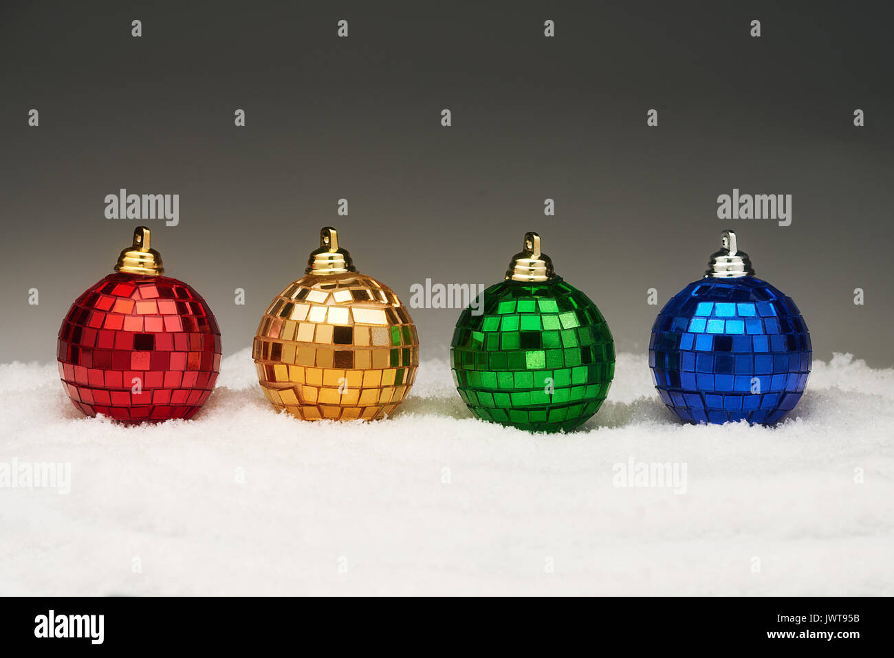 Four color christmas balls in a row in snow on gray background with ...