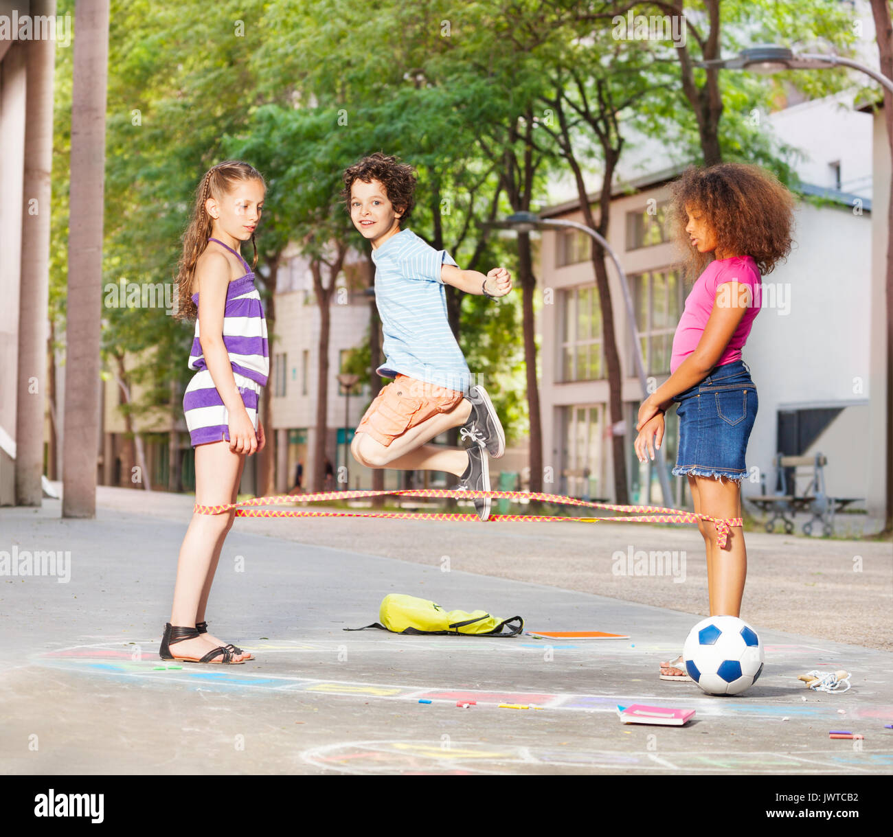 Boy jumps with friends after school over elastic robe playing yoki game ...