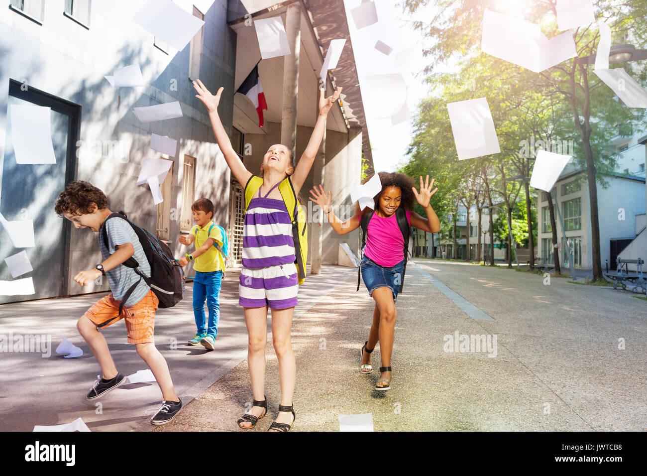 Group of friends schoolkids throwing paper sheets in the air with ...