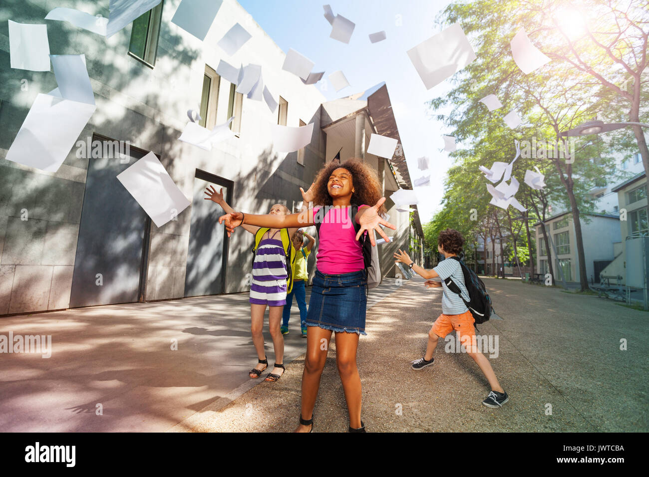 Happy African girl with curly hair throws papers in the air and friends ...