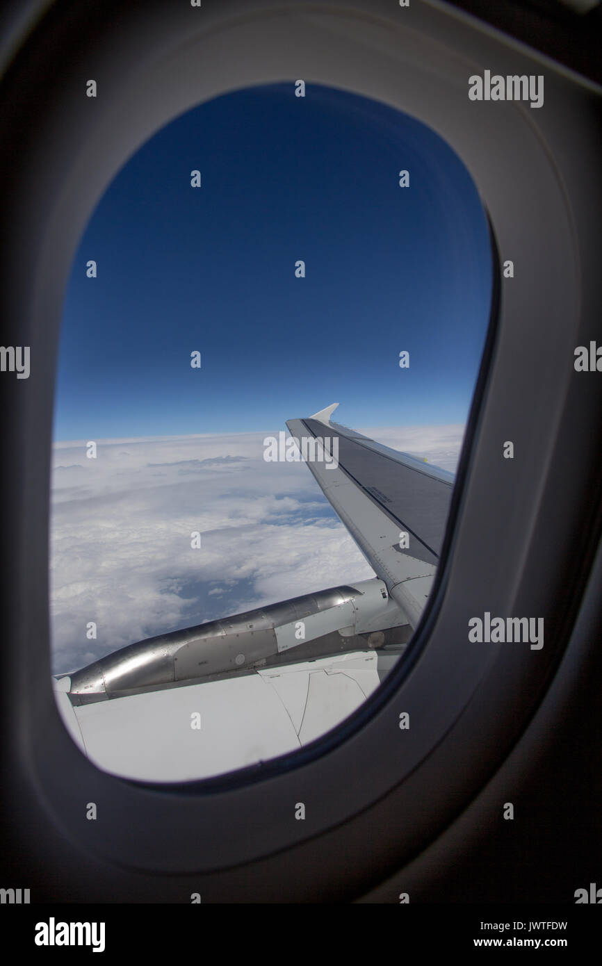Vertical view of airplane window and the wing with clouds below and ...