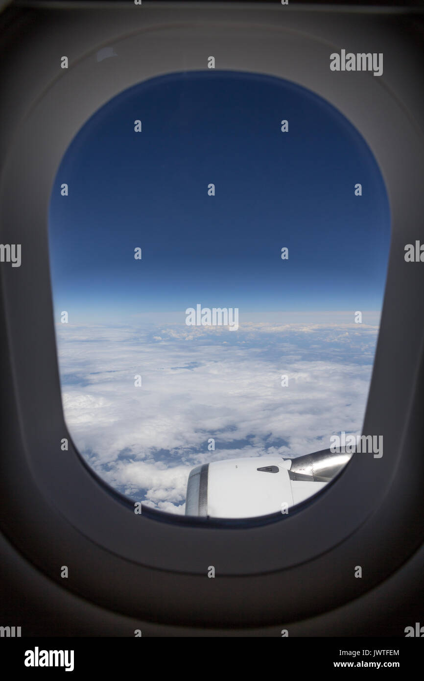 Vertical view of plane window with light, white clouds and blue sky and ...